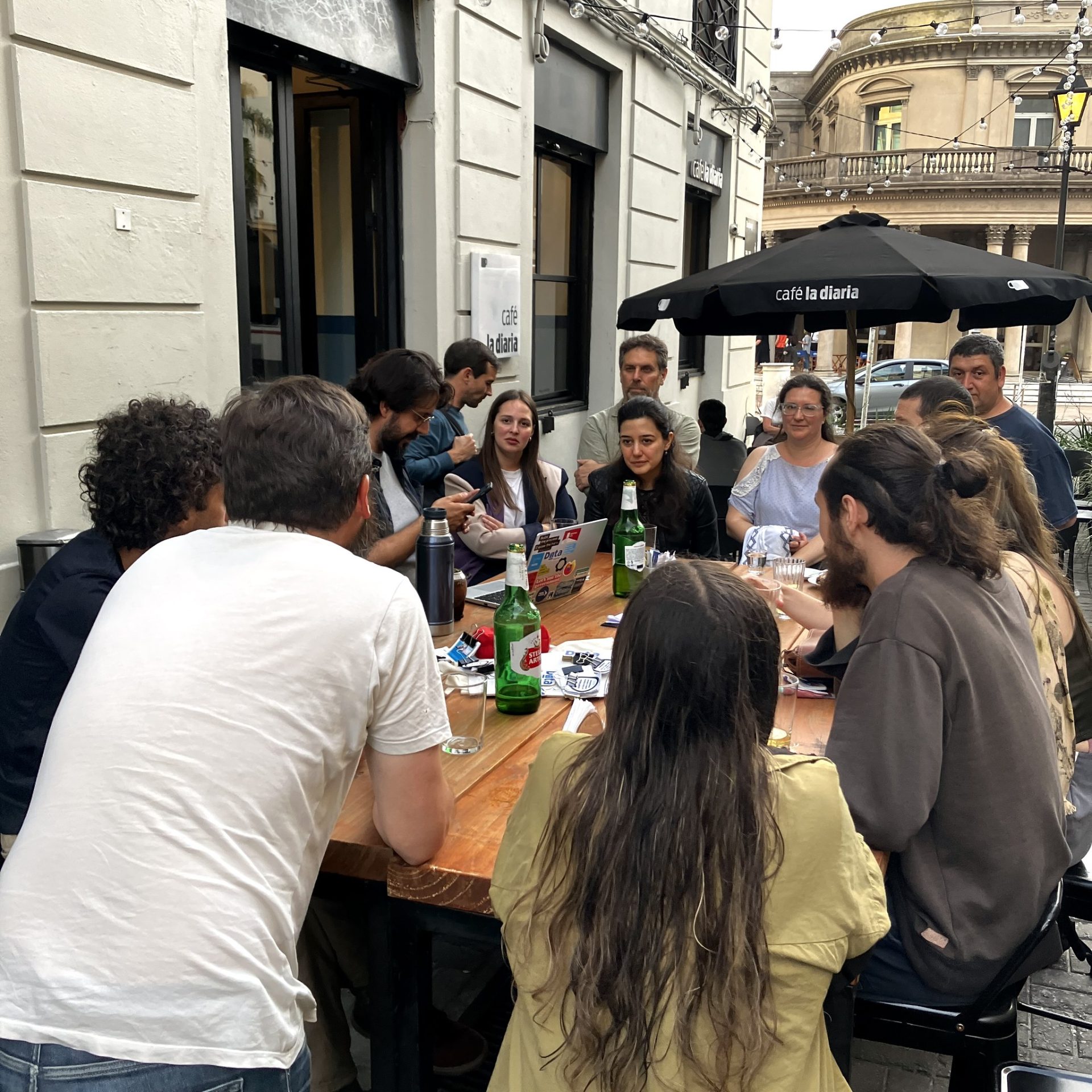 Grupo de personas alrededor de una mesa alta, sentadas en banquetas, charlando en el Datos y Cogollos, en café la diaria.